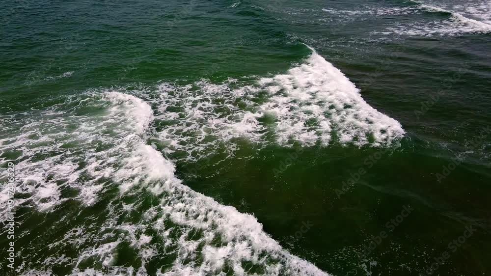 A close-up aerial view of the ocean surface reveals white foam from ...