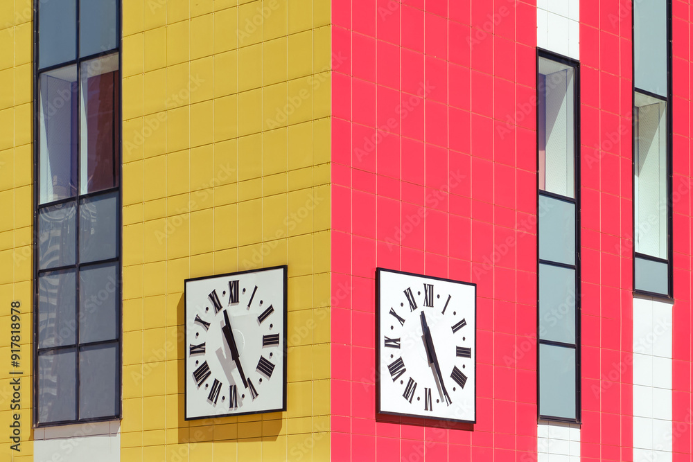 Two clock faces on the corner of a building with yellow and red facades ...