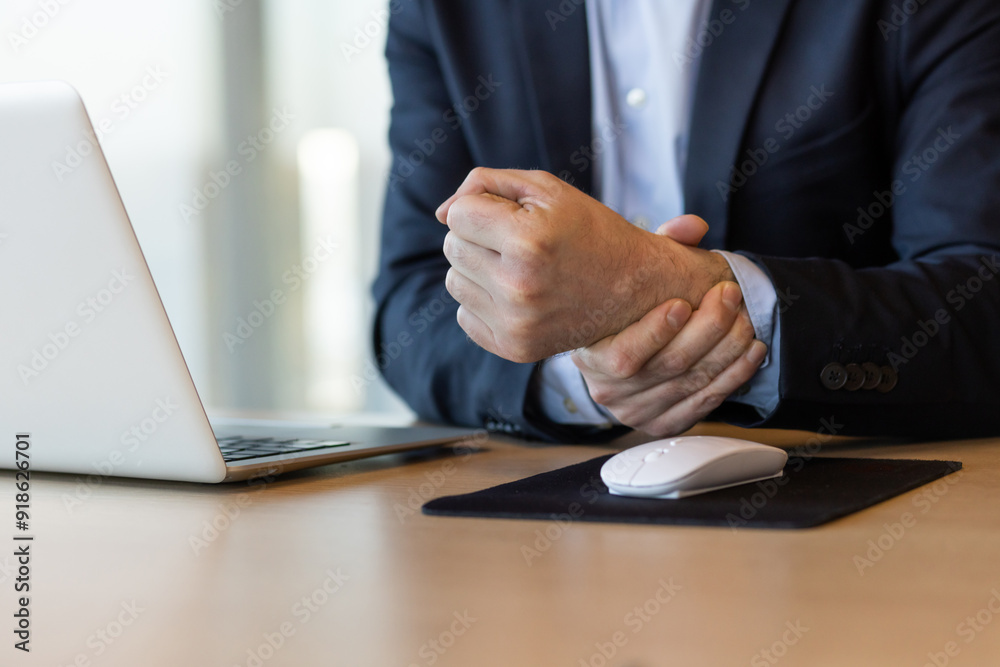 Businessman experiencing wrist pain while working on laptop at desk ...