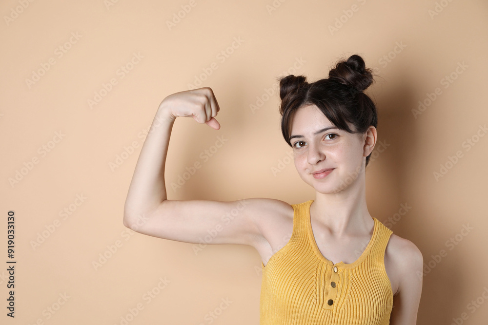 Poster Portrait of cute teenage girl showing muscles on beige ...