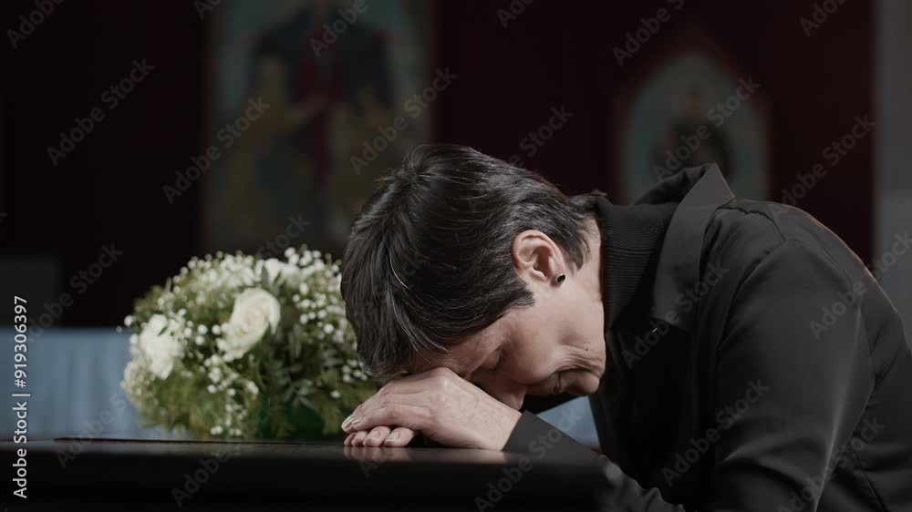 Caucasian woman wearing black suit putting head on hands over coffin ...