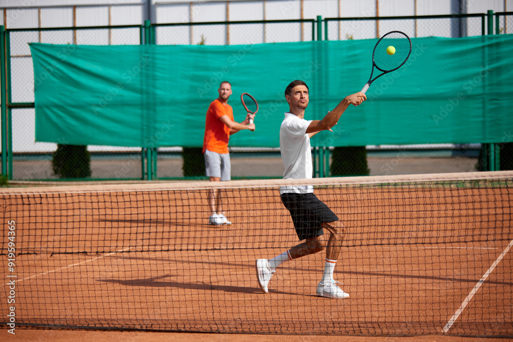 Two men, friends spending active time on outdoor tennis court, playing ...