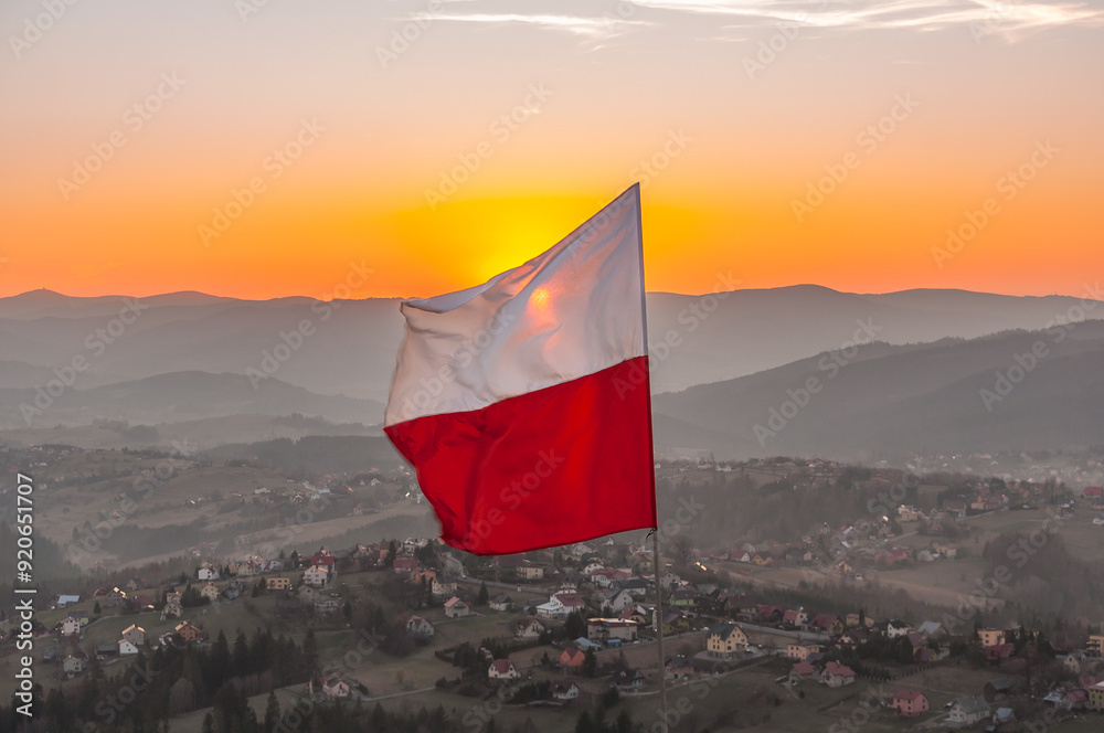 Biało-czerwona flaga Polski na tle zachodzącego słońca w górach ...