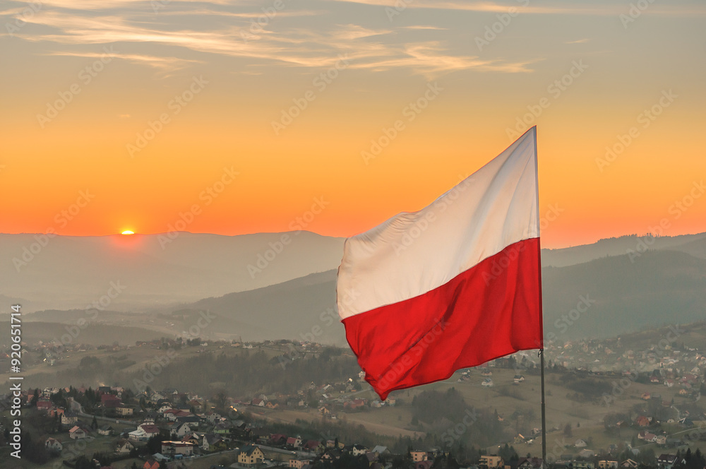 Biało-czerwona flaga Polski na tle zachodzącego słońca w górach ...