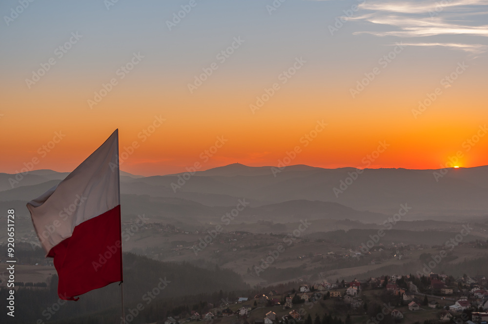Biało-czerwona flaga Polski na tle zachodzącego słońca w górach ...