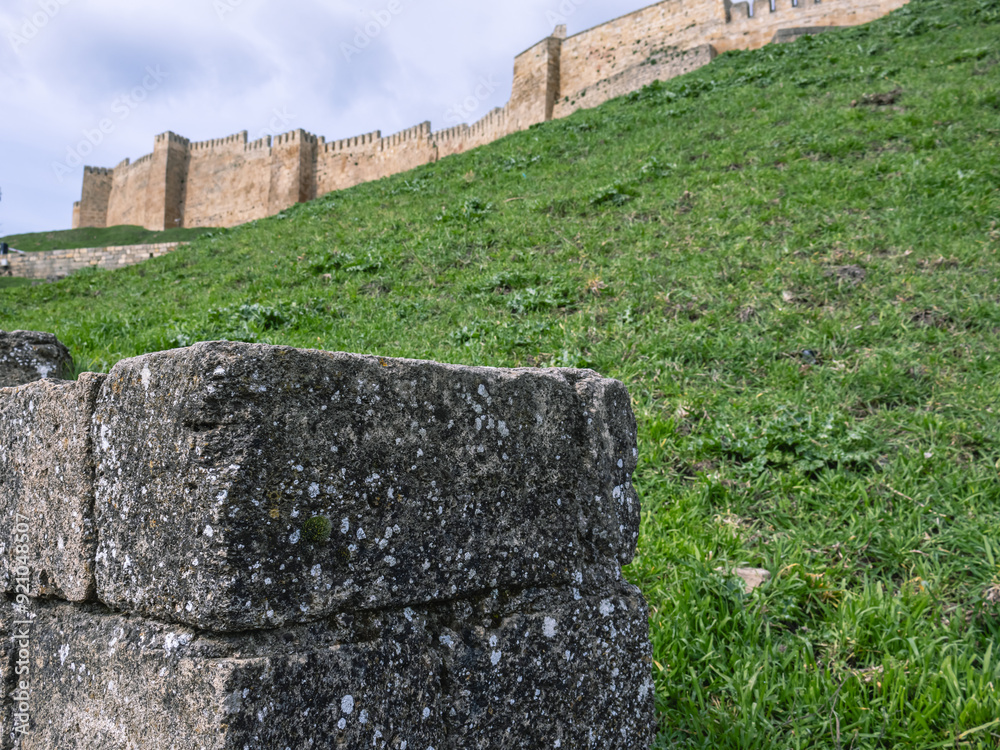 Ancient stone blocks form a wall. An ancient fortress is visible behind ...