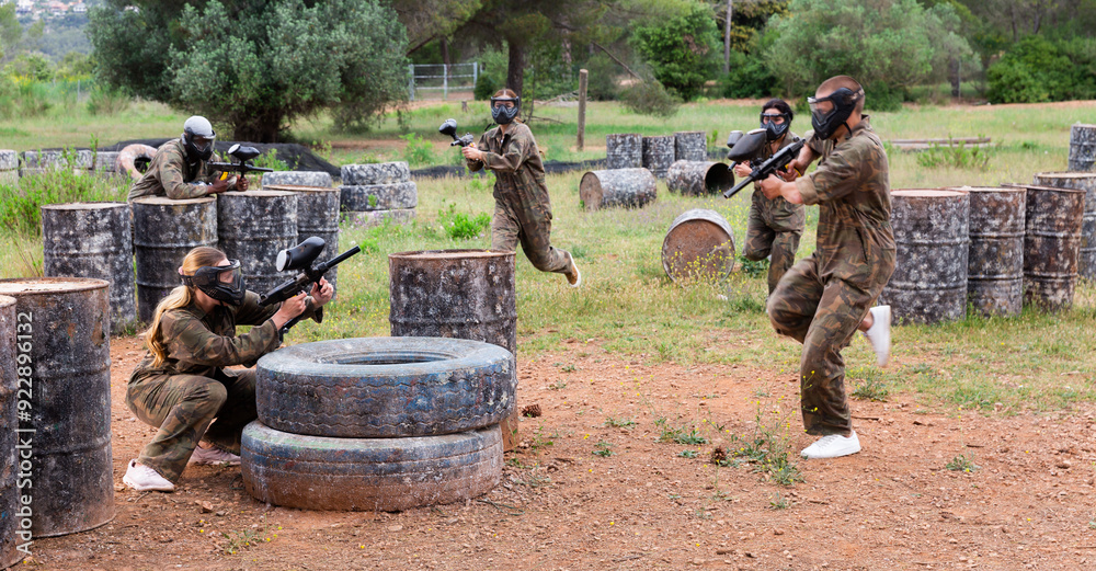 Dynamic paintball battle, players jumping and aiming with guns outdoors ...