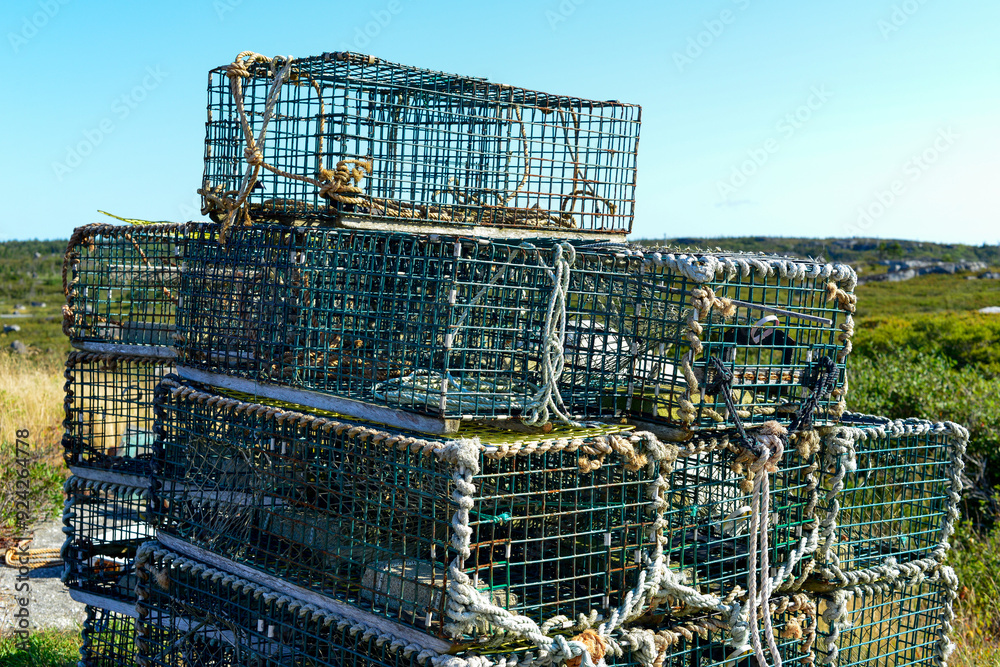 Multiple green lobster pots or traps are stacked high along a fishing ...