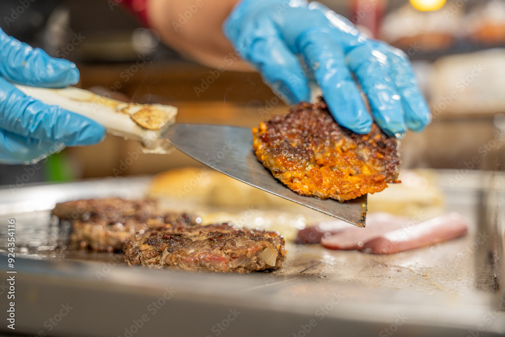 Cook preparing hamburger on griddle in fast food restaurant kitchen ...