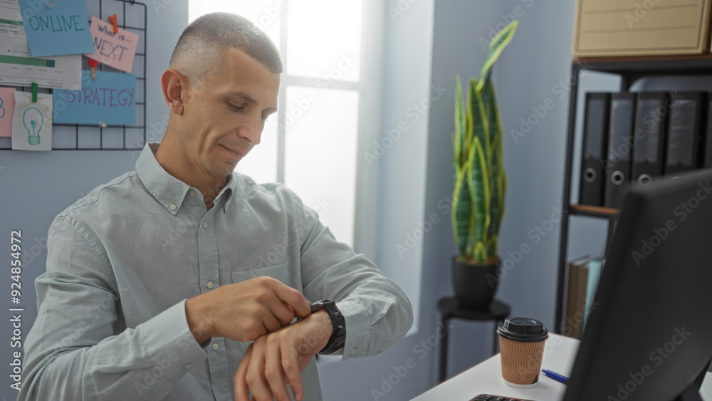 Man in an office checks his smartwatch while seated at a desk with ...