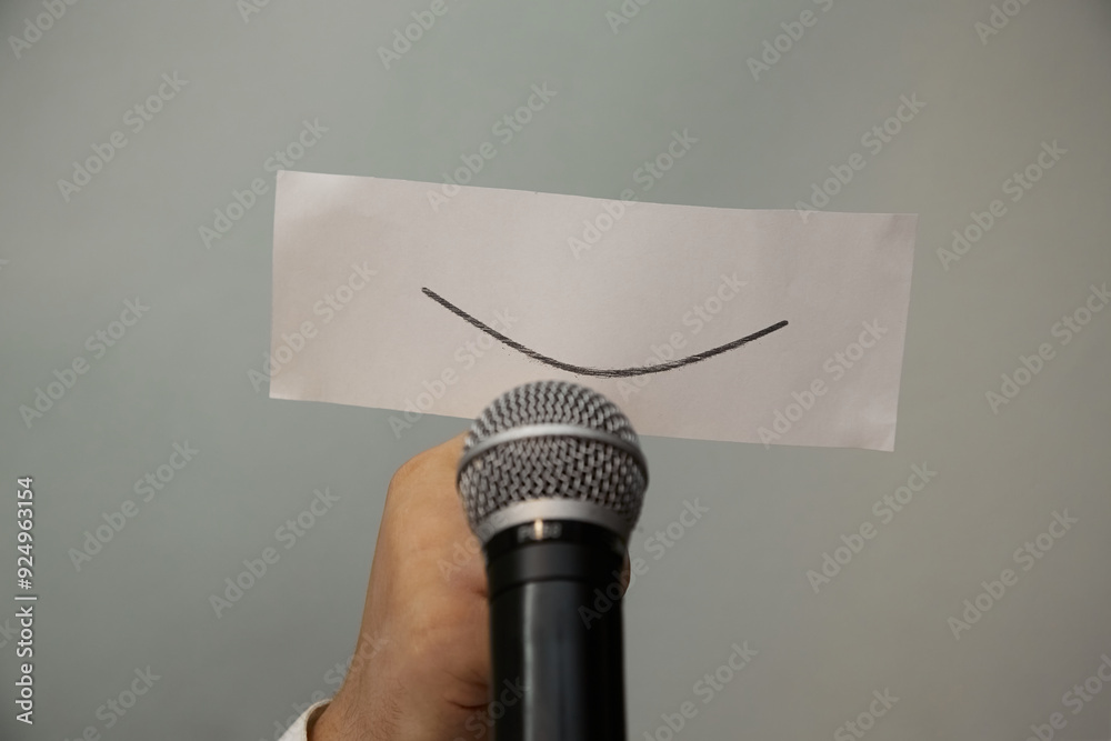 A hand holding a drawn smile in front of a microphone, a person hiding ...