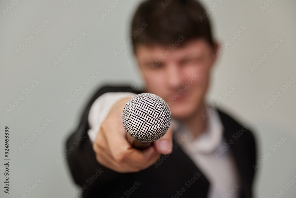 Blurred image of a young man pointing a microphone at the viewer ...