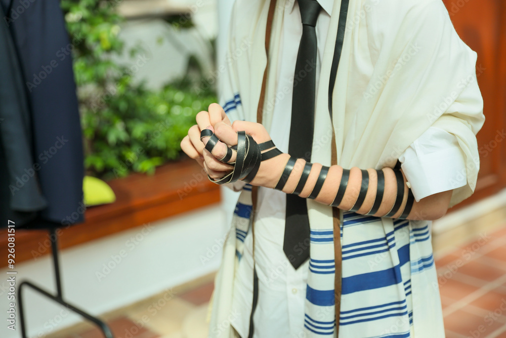 Man wrapping tefillin on his arm for a Jewish prayer ceremony, wearing ...