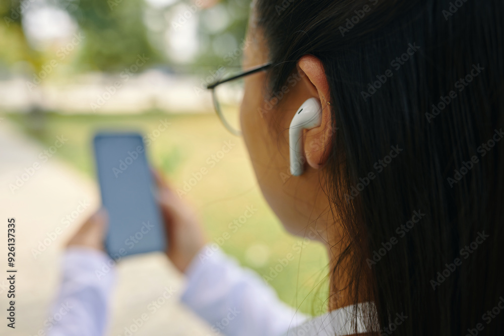 Person holding smartphone while wearing wireless earbuds in outdoor ...