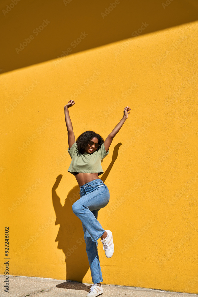 Happy young African American woman winner jumping standing at yellow ...