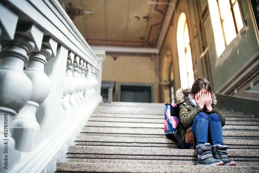 Portrait of bullied girl is crying on the steps in front of the school ...