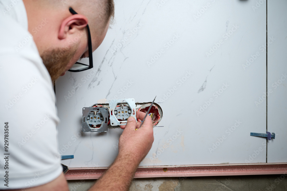 Professional electrician installing electric socket into the wall using ...