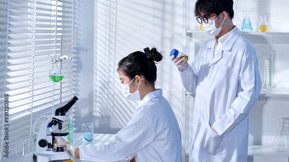 In a modern laboratory, two scientists are monitoring chemical tanks ...