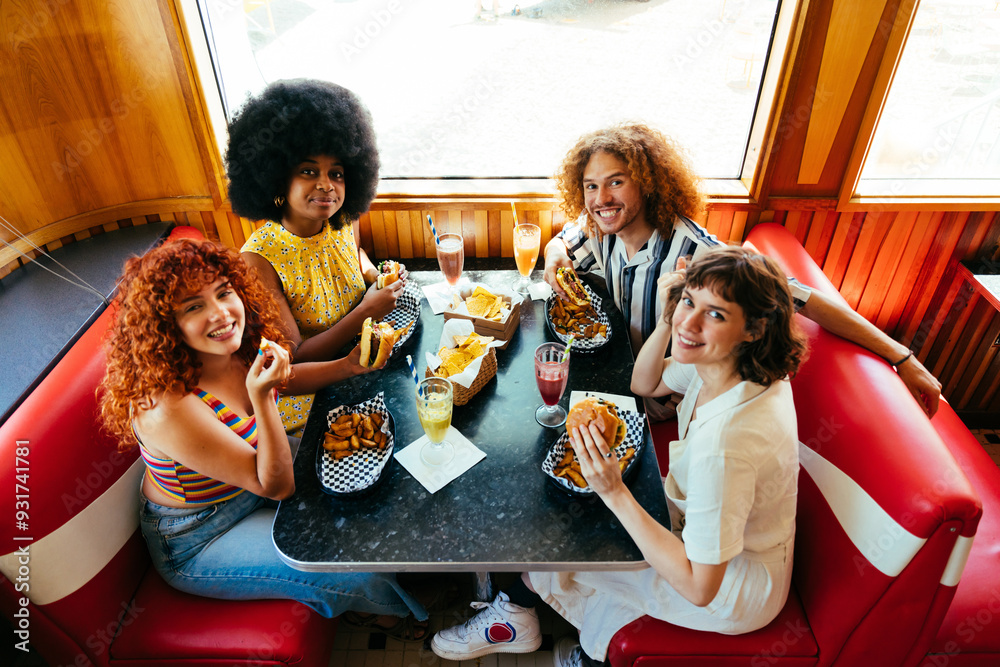 Multiethnic group of friends having meal at 80s vintage diner ...