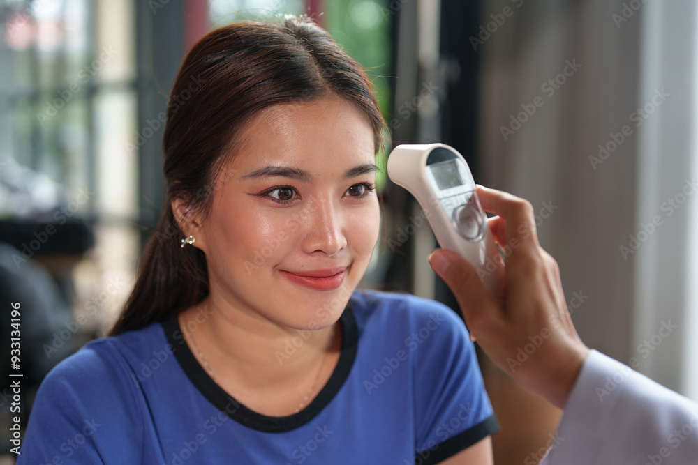 Asian female doctor uses infrared forehead thermometer to check woman's ...