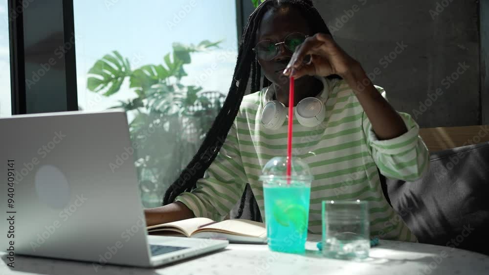 Young woman student with dreadlocks puts straw into cup with turquoise ...
