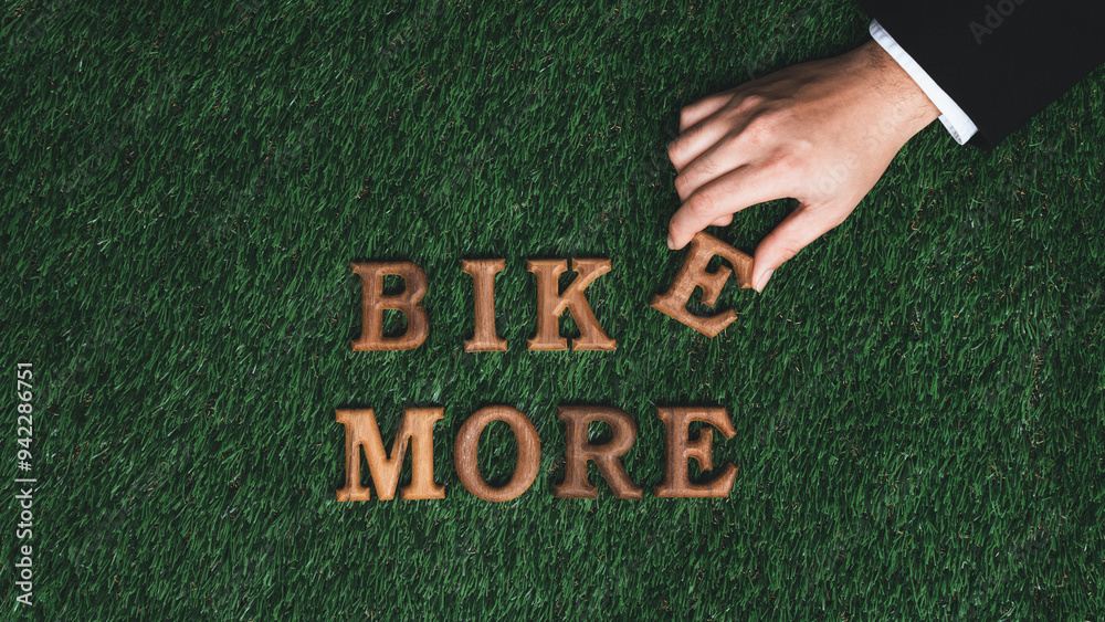 Hand arrange wooden alphabet text in BIKE MORE on green biophilic grass ...