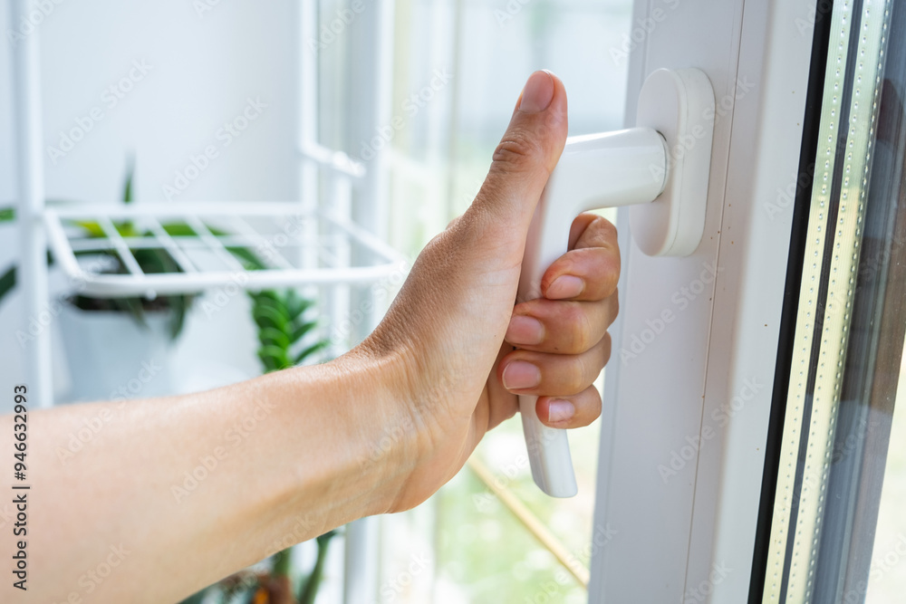 The hand holds the handle of a plastic double-glazed window, closing ...