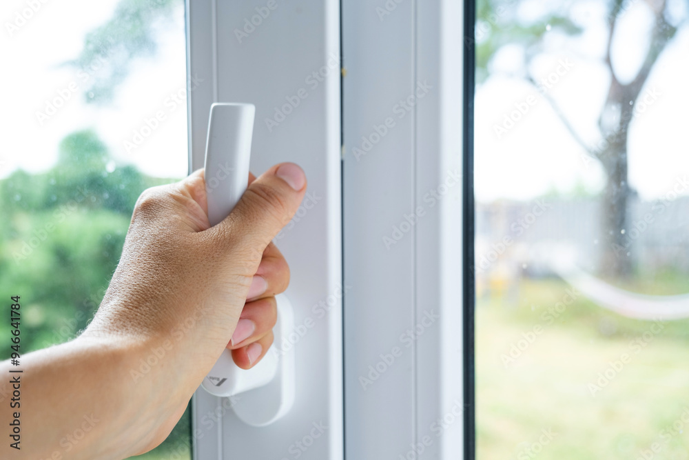 The hand holds the handle of a plastic double-glazed window, closing ...