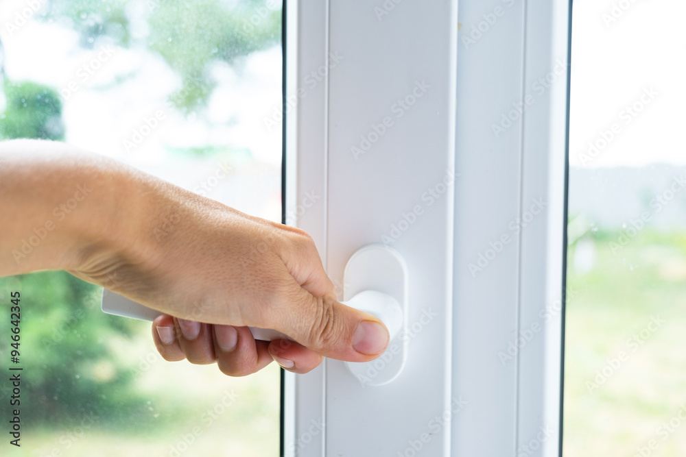 The hand holds the handle of a plastic double-glazed window, closing ...