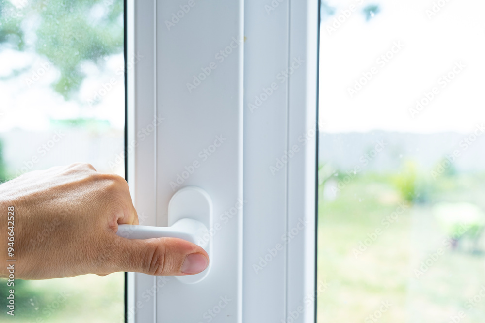 The hand holds the handle of a plastic double-glazed window, closing ...