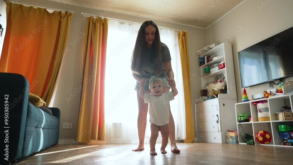 Mother helps son walk barefoot at home. son taking steps indoors with mother support. Mother ...