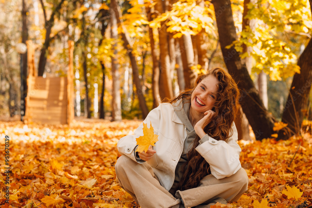 Smiling girl sits in the autumn foliage on the ground of the forest ...