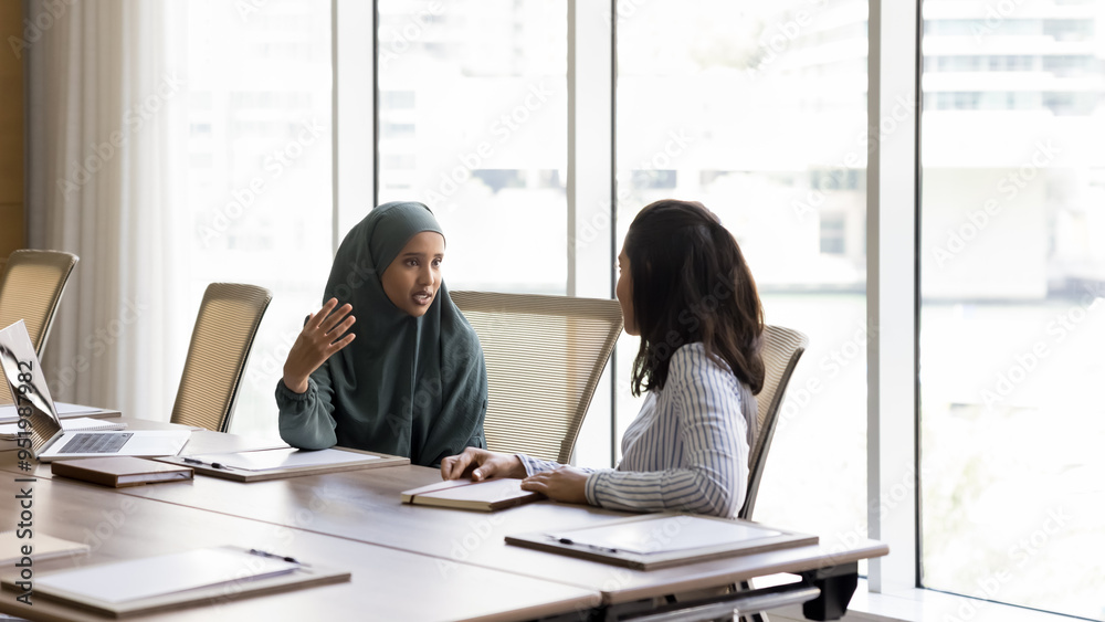 Serious young Arab manager woman in hijab talking to female business ...