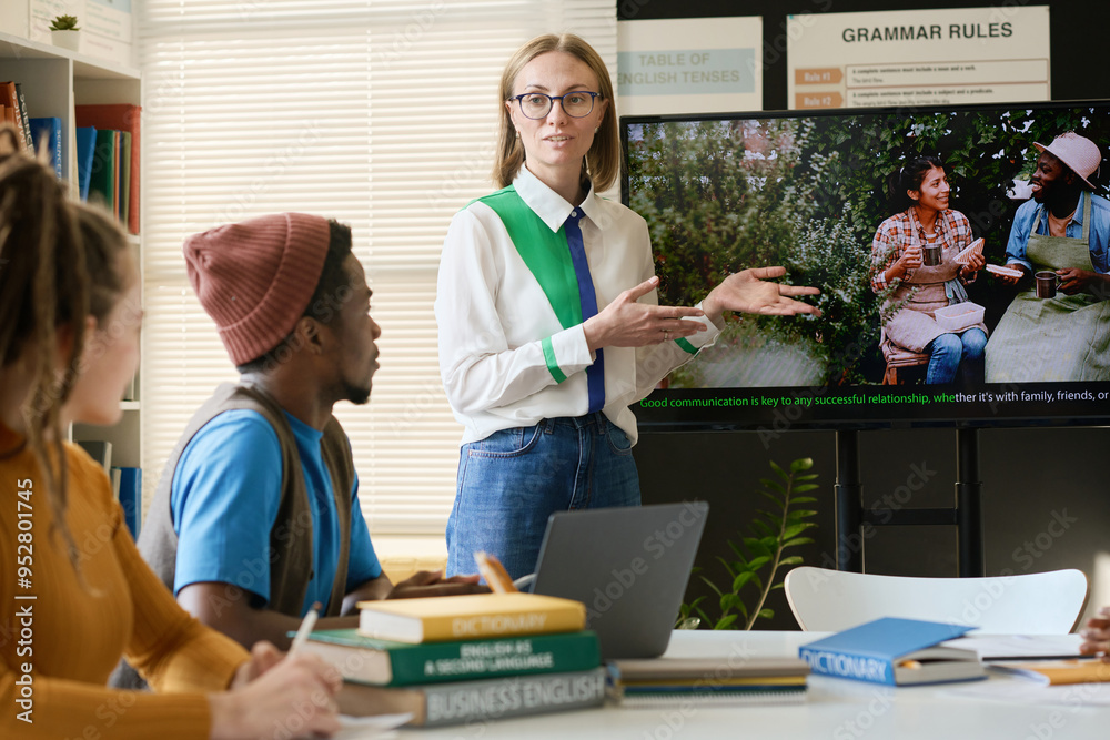 Young female teacher pointing at screen and showing video on TV to ...