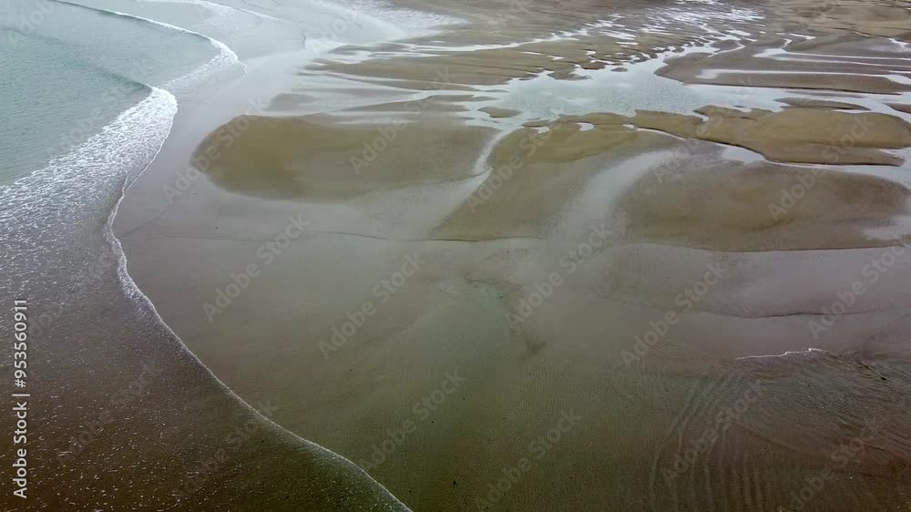 An aerial view of a sandy beach with receding water revealing intricate ...