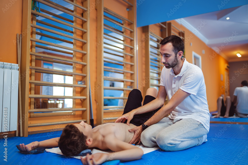 Therapeutic exercise kinesitherapy of little boy. Straightening the spine while the boy is lying ...