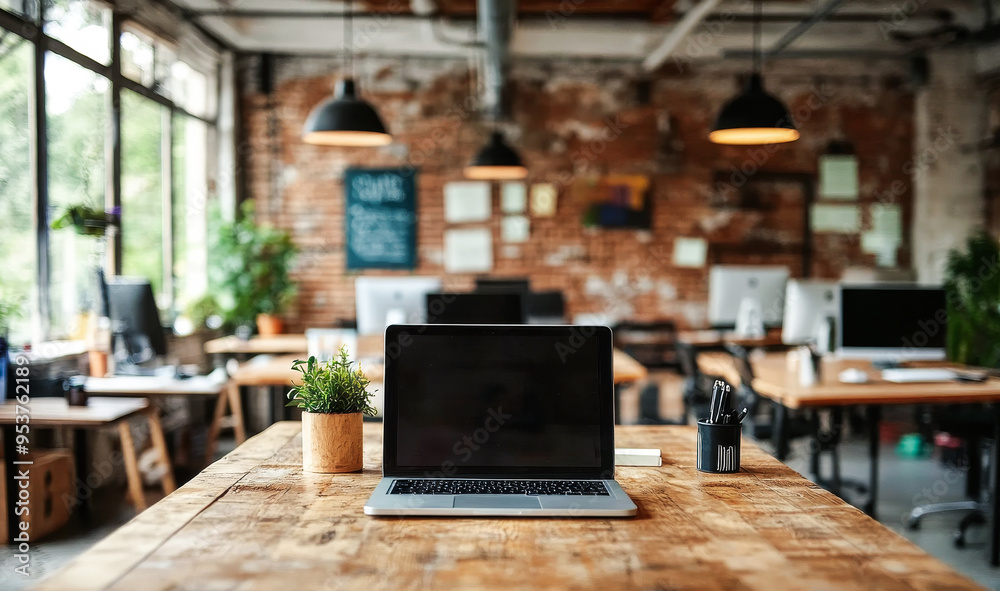 Open laptop computer is sitting on a desk in a busy open plan office ...