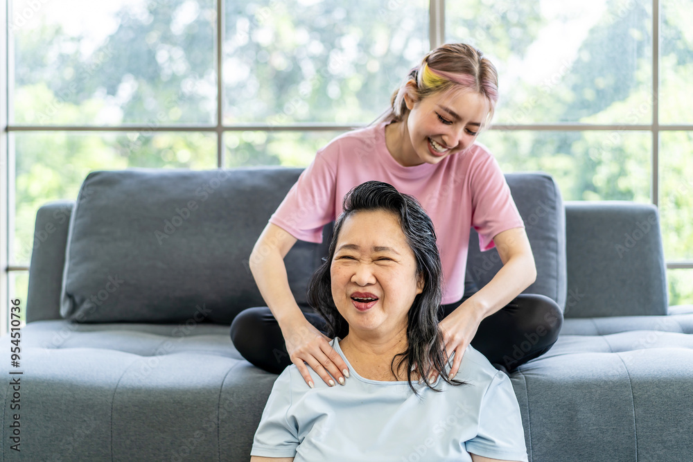 Young Asian daughter massages shoulder, relieves pain of elderly Asian mother while sitting on ...