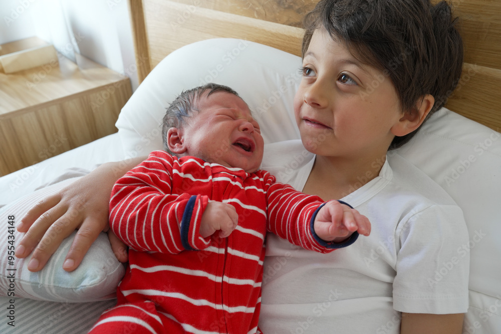 Older brother holding his crying newborn sibling in a striped red ...