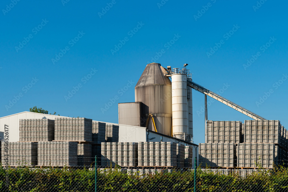 Industrial site with a tall silo and conveyor and stacked concrete ...