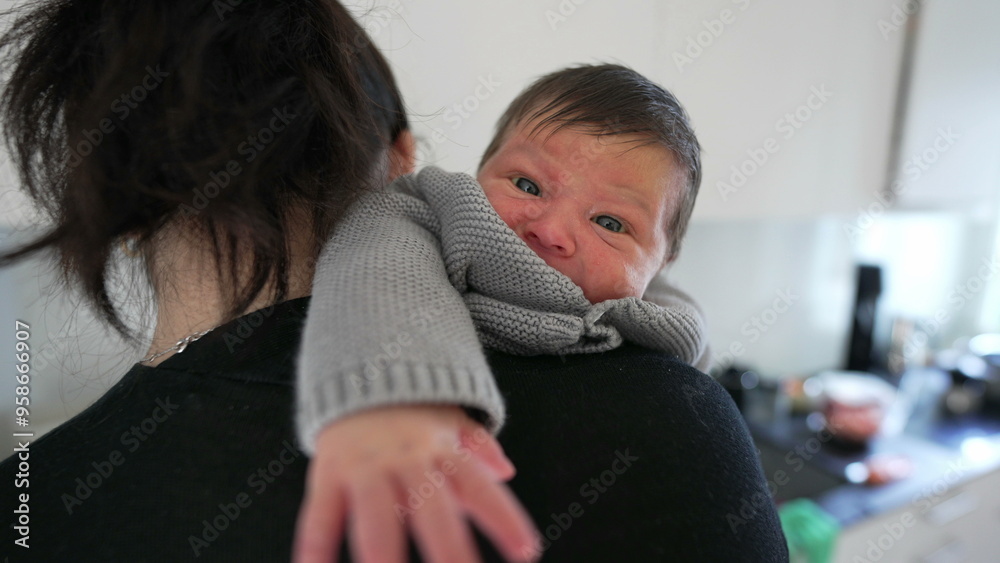 Baby with expressive face looks over mother’s shoulder, close-up shot ...