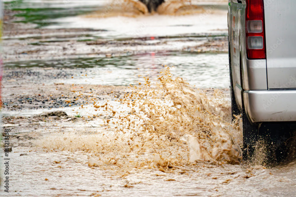 A car is driving through a flooded street with water splashing up from ...