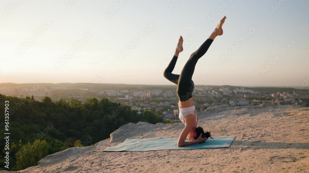 Woman practices yoga on cliffside at sunset, performing headstand ...