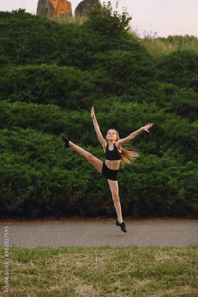 Little girl in black top and shorts doing splits in the air on nature ...
