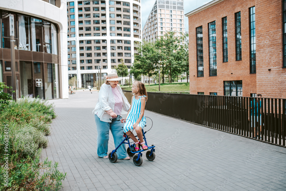 Grandma with walker and granddaugter in the city, on walk. Girl ...