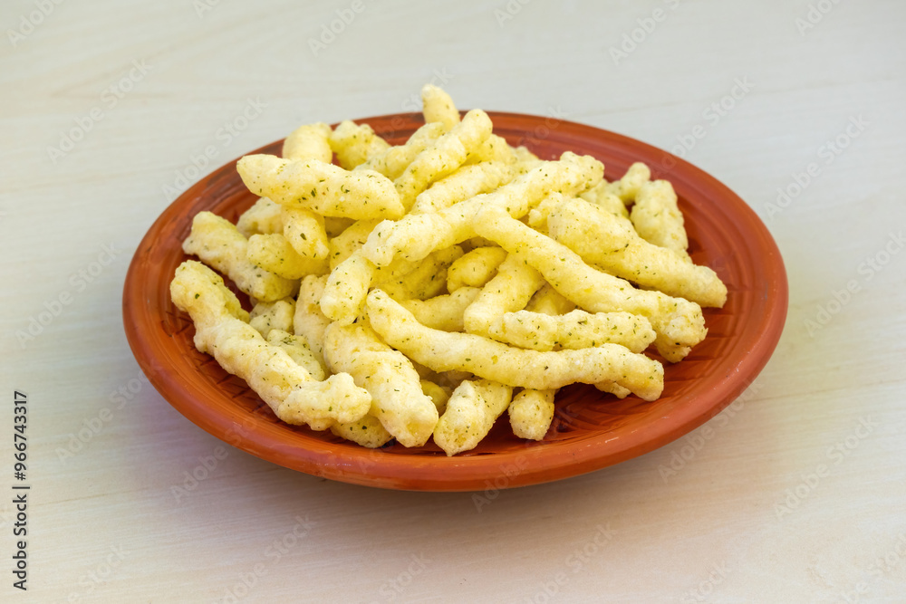 Delicious corn stick chips in a clay plate on a light wooden surface ...
