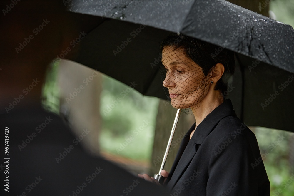 Side view of senior woman in black suit and veil grieving over loss of ...