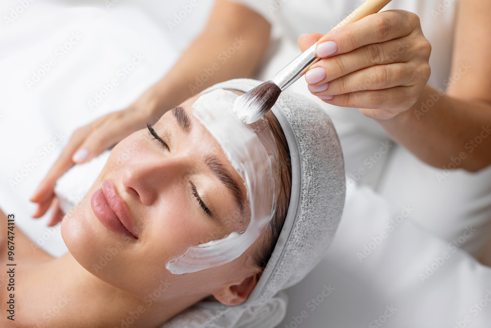 Spa specialist holding brush and making white nourishing mask to lovely ...