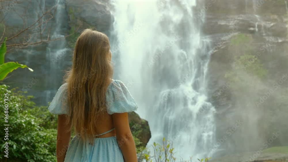 Woman with long hair standing in front of majestic waterfall surrounded ...