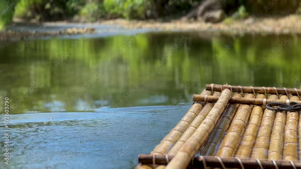 A Thai person is using a bamboo stick to steer a bamboo raft down a ...